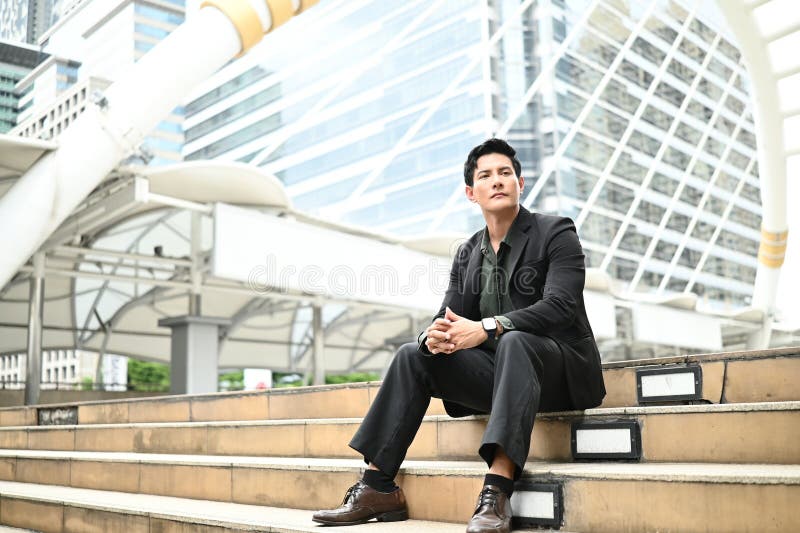 A Man in a Suit Sits on a Set of Steps in Front of a Large Building. he ...