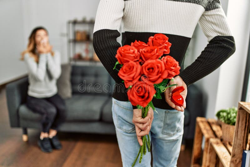 Man Suprising Woman With Bouquet Of Roses And Engagement Ring At Home