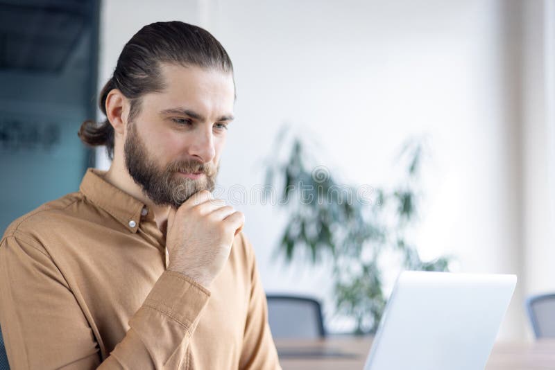 Man Thoughtfully Working on His Laptop in a Bright Modern Office Stock ...