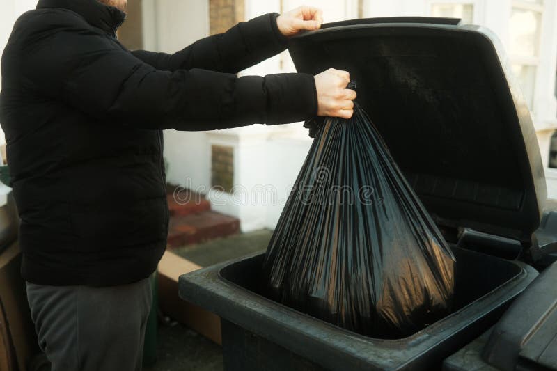 A Man Throwing a Black Garbage Bag into an Outdoor Trash Bin Stock ...