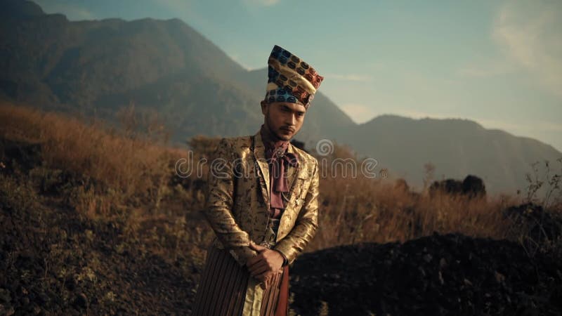 Man in Traditional Attire Standing in a Field with Mountains in the ...