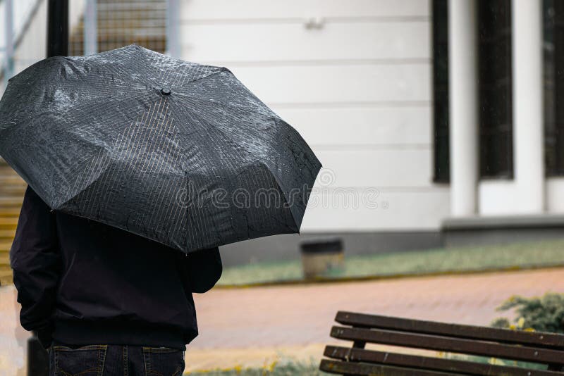 A Man Under an Umbrella at a Bus Stop Waiting for a Bus on a Rainy Day ...