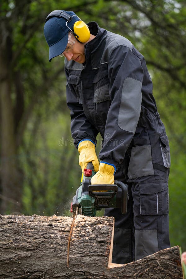 A Man in Uniform Cuts an Old Tree in the Yard with an Electric Saw ...