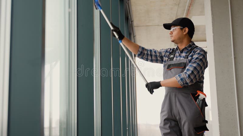 A Man in Uniform Washes a Windows with Scraper. Professional Home or ...