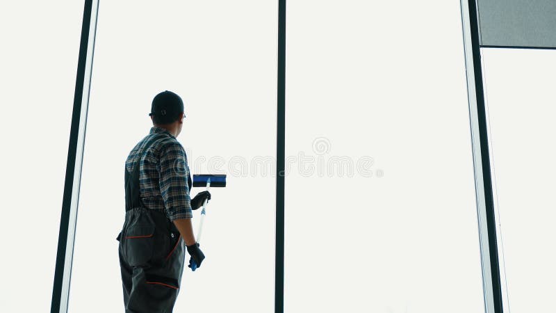 A Man in Uniform Washes a Windows with Scraper. Professional Home or ...