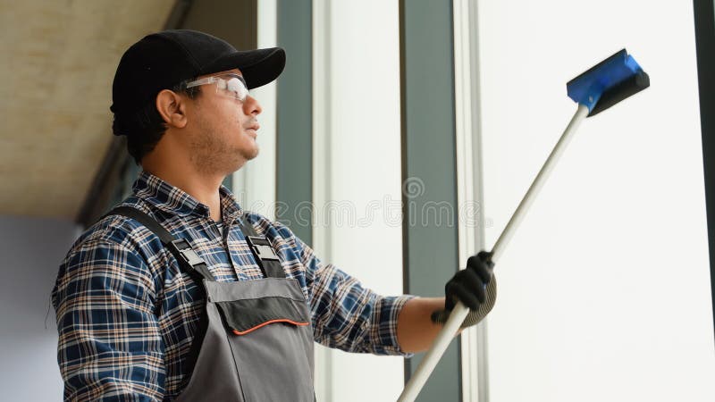 A Man in Uniform Washes a Windows with Scraper. Professional Home or ...