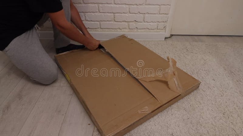 A Man Unpacks a Book Shelf. Tears the Cardboard Packaging Stock Footage ...