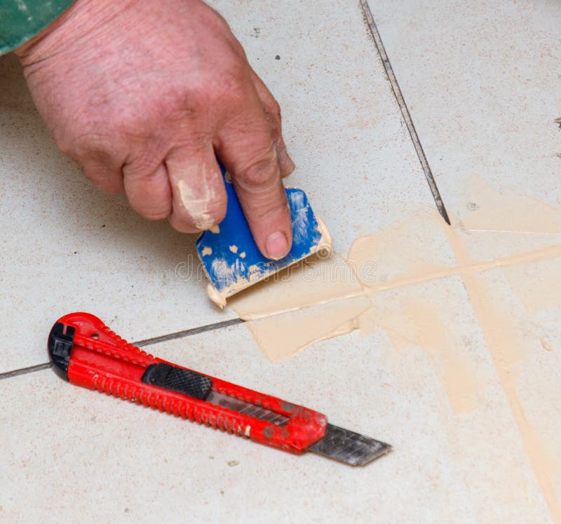 A Man is Using a Blue Putty Knife To Apply a Patch To a Tile Stock ...