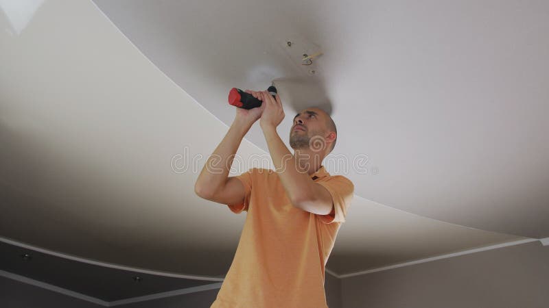 A Man Drills Holes in the Ceiling with a Portable Drill To Install a ...