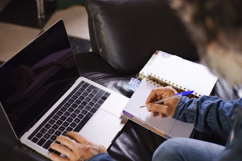 Man Using Laptop and Writing Notes in a Notebook and on the Sofa at ...