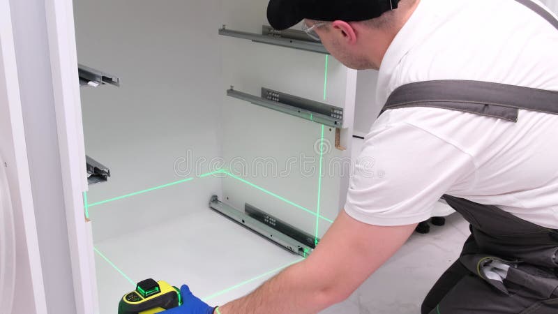 A Man Using a Laser Level To Install a Drawer in a Kitchen Cabinet ...