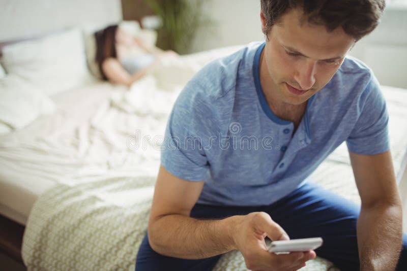 Man Using Mobile Phone while Woman Sleeping on Bed Stock Image - Image ...