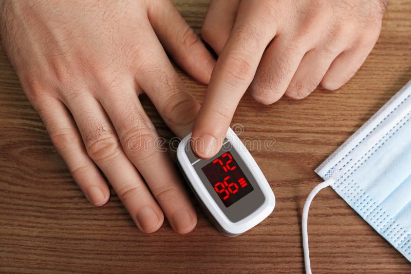Man Using Pulse Oximeter for Oxygen Level Testing at Wooden Table with ...