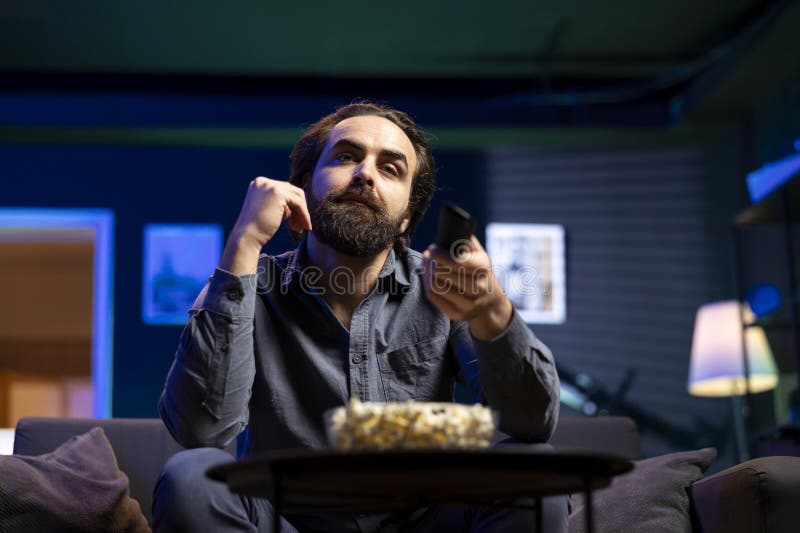 Man Using Remote Control To Switch Channels on TV while Eating Popcorn ...