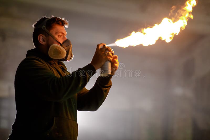 Man Using a Spray Can To Create Flames in an Industrial Setting at Night with Dramatic Lighting ...