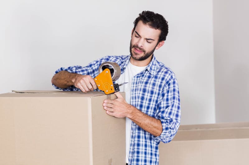 Man Using Tape Dispenser Sealing Large Cardboard Box in Empty Room with ...
