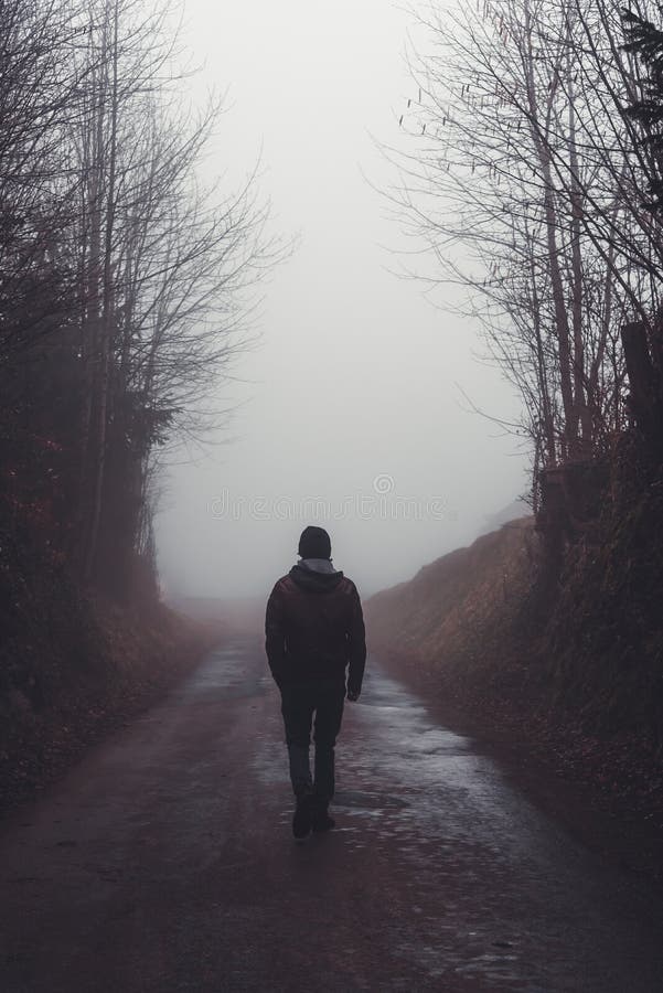 Man Walking Alone On A Road Through A Dark Foggy Forest Stock Image Image Of Forest Mist