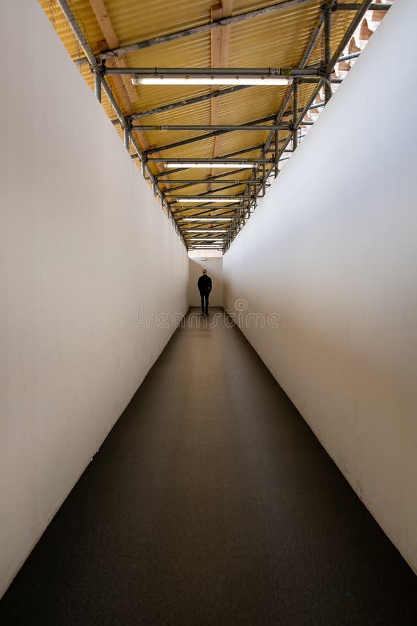 Man Walking Down a Corridor Towards a Well Lit End Exit Stock Image ...