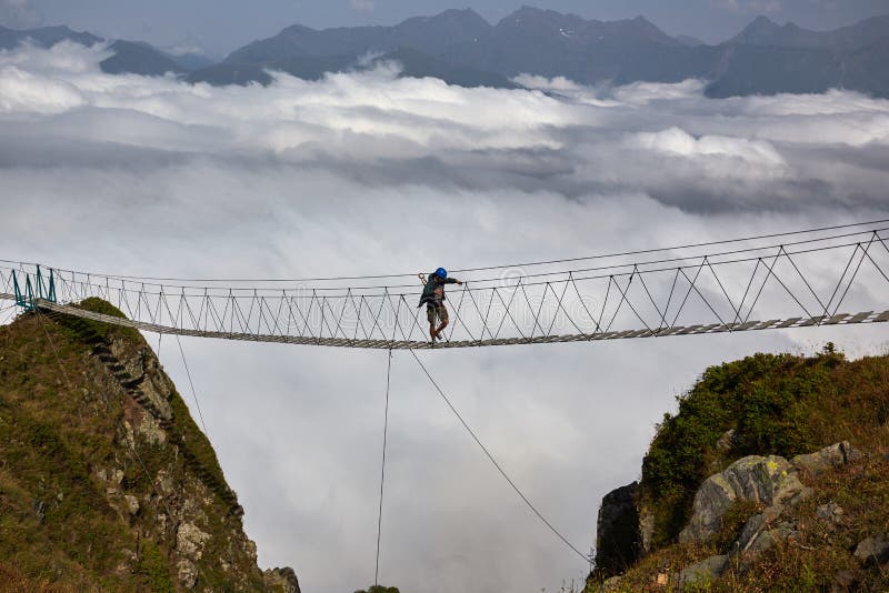 Man Walking on Suspension Bridge and Looking at Cloudy Mountains Below ...