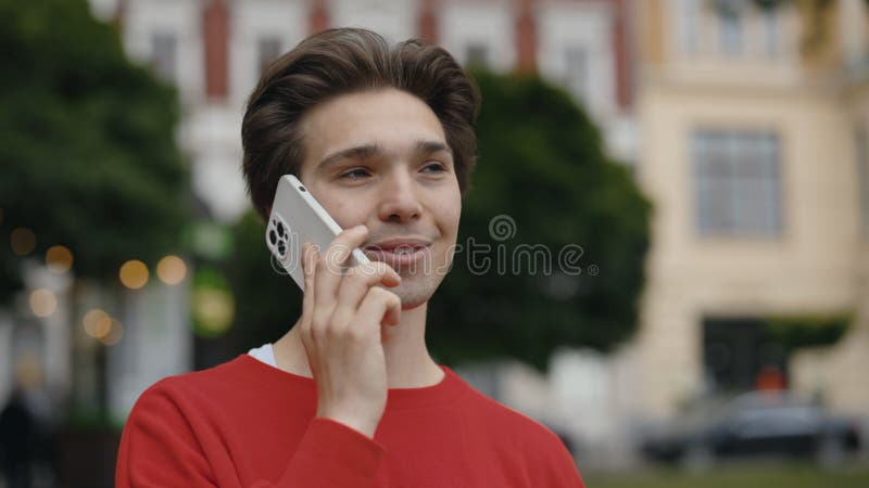 A Smiling Young Man Walks Down The Street Talking On His Phone