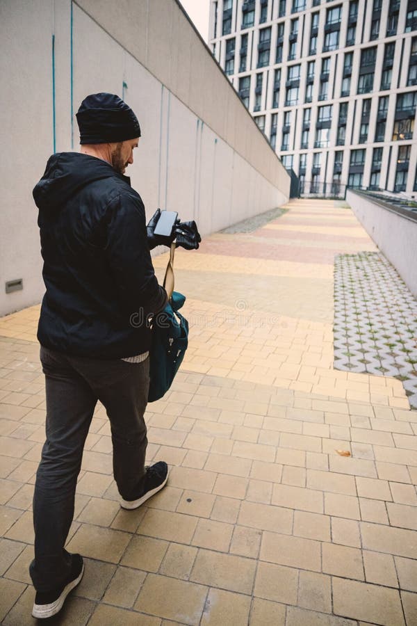 A Man Walks Against the Backdrop of Modern Urban Architecture. he is ...