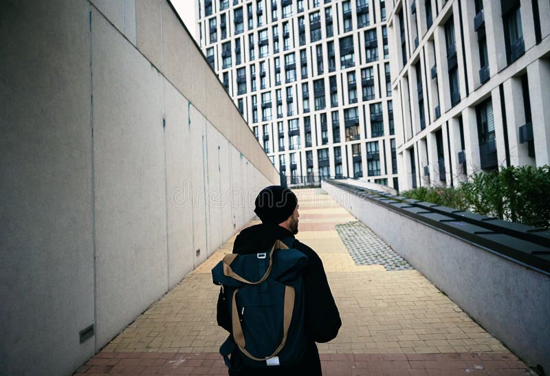 A Man Walks Against the Backdrop of Modern Urban Architecture. he is ...