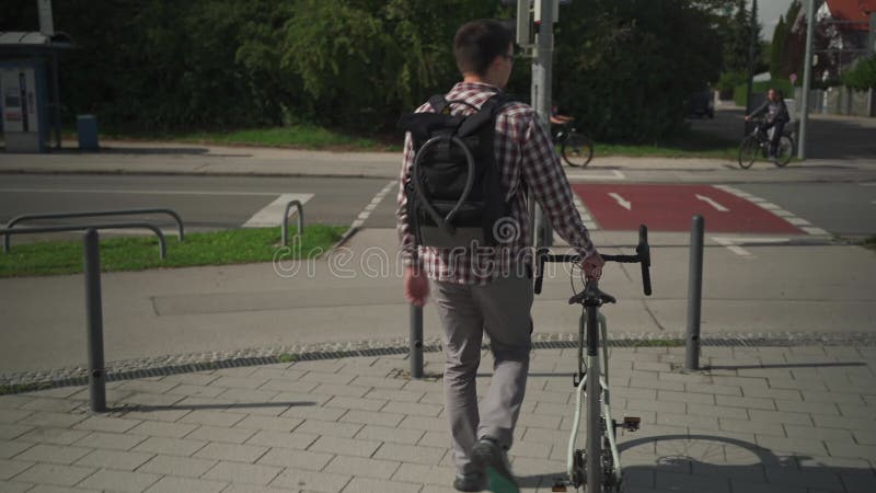 Man Walks Next To Bicycle with Backpack on Which Hangs Cycle Lock. Back ...