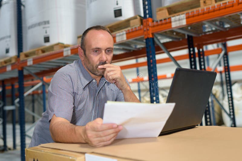 Man in Warehouse with Laptop Looking at Papers Stock Image - Image of ...