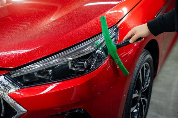 A Man Washes the Headlights of a Red Car with a Scraper. Stock Image ...