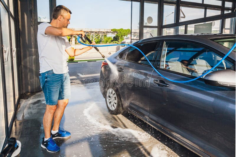 A Man Washes His Car at a Self-service Car Wash Using a Hose with ...