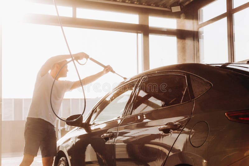 A Man Washes His Car at a Self-service Car Wash Using a Hose with ...