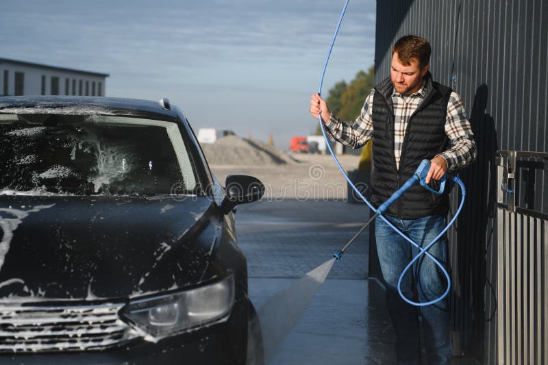 A Man Washes His Car at a Self Service Car Wash Using a Hose with ...