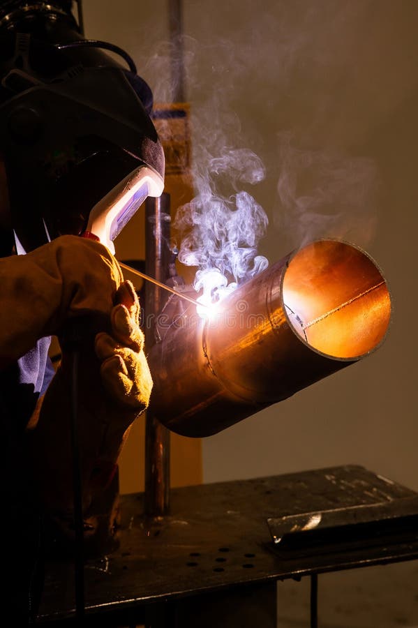 A Man Wearing a Protective Mask Welds a Metal Pipe. Stock Photo - Image ...