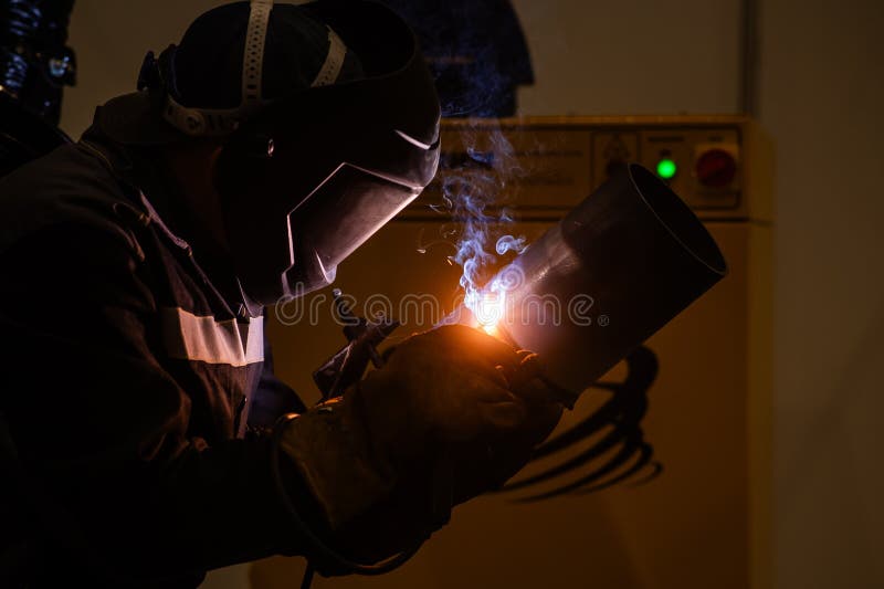 A Man Wearing a Protective Mask Welds a Metal Pipe. Stock Photo - Image ...
