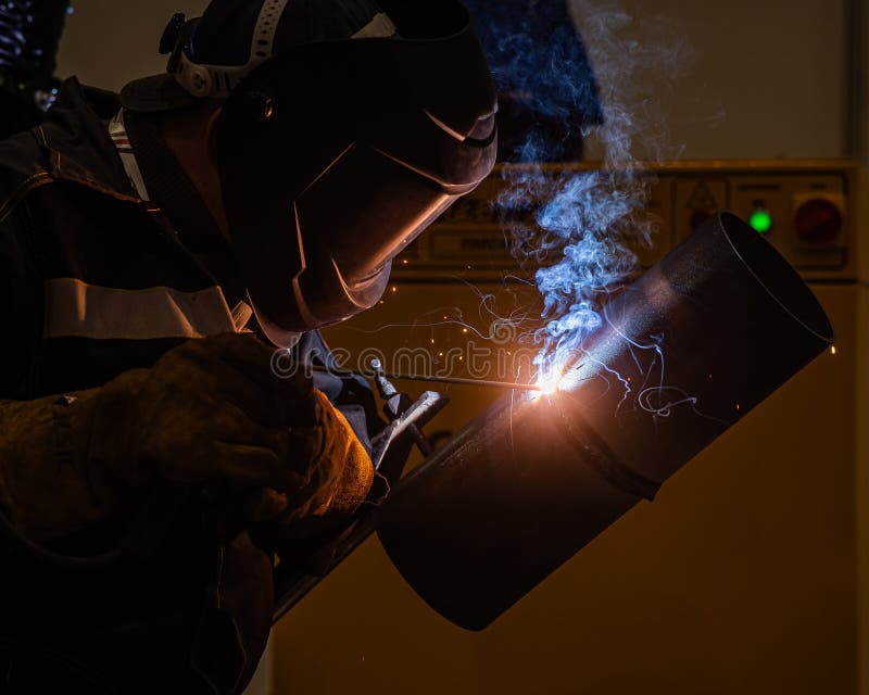 A Man Wearing a Protective Mask Welds a Metal Pipe. Stock Photo - Image ...