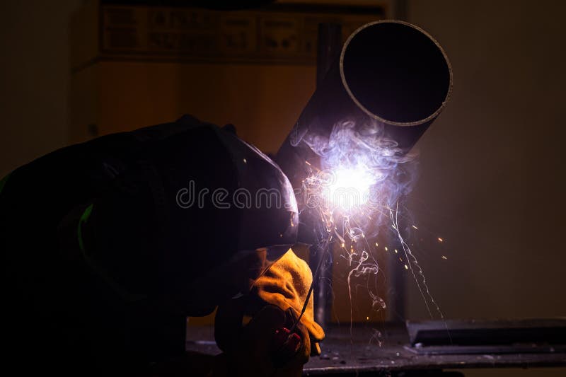 A Man Wearing a Protective Mask Welds a Metal Pipe. Stock Photo - Image ...