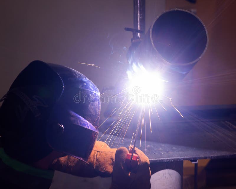 A Man Wearing a Protective Mask Welds a Metal Pipe. Stock Photo - Image ...