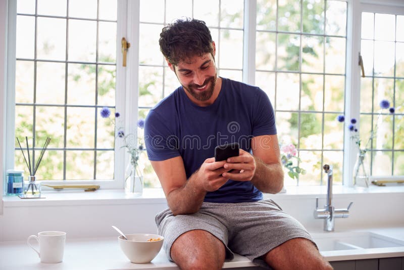 Man Wearing Pyjamas in Kitchen Using Mobile Phone Whilst Eating ...