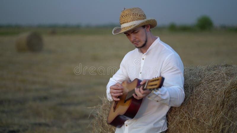 Man Wearing a Straw Hat Playing the Guitar about a Haystack Stock ...
