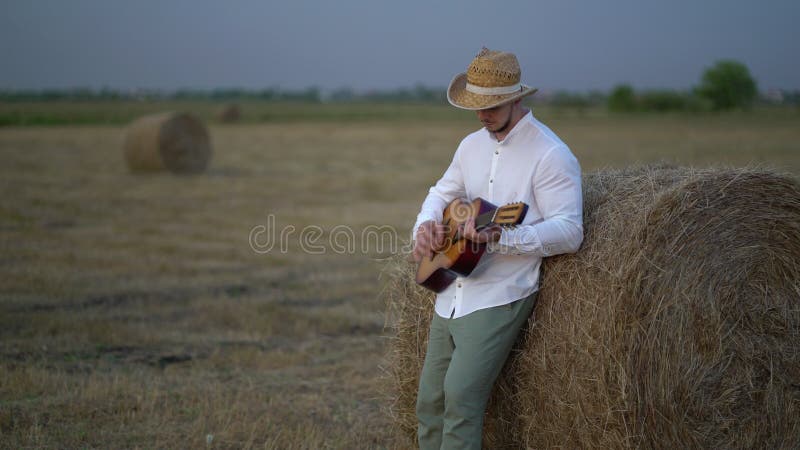 Man Wearing a Straw Hat Playing the Guitar about a Haystack Stock ...