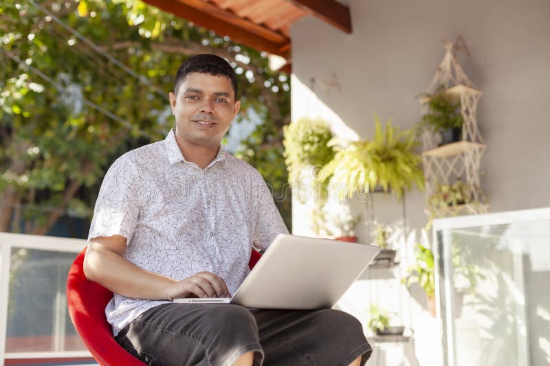 Man in a White Shirt Using a Computer on a Balcony with Green Space in ...