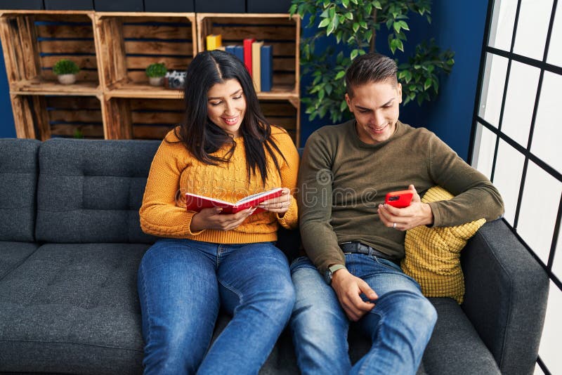 Man and Woman Couple Using Smartphone and Reading Book at Home Stock ...