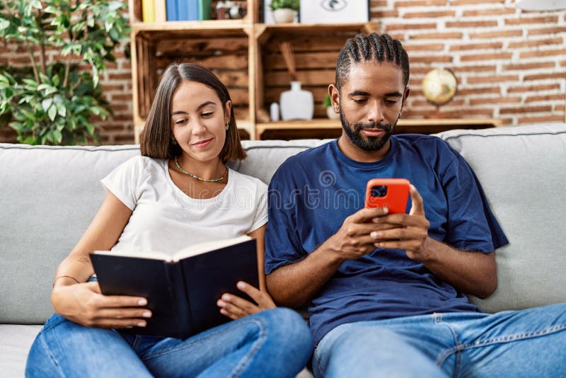 Man and Woman Couple Using Smartphone and Reading Book at Home Stock ...