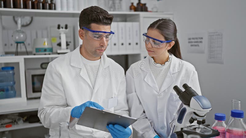 Man and Woman in Lab Coats Examine Data on a Tablet Inside a Science ...