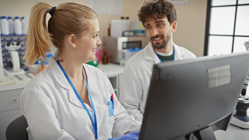 Man and Woman in Lab Coats Smiling at Each Other by a Computer in a ...