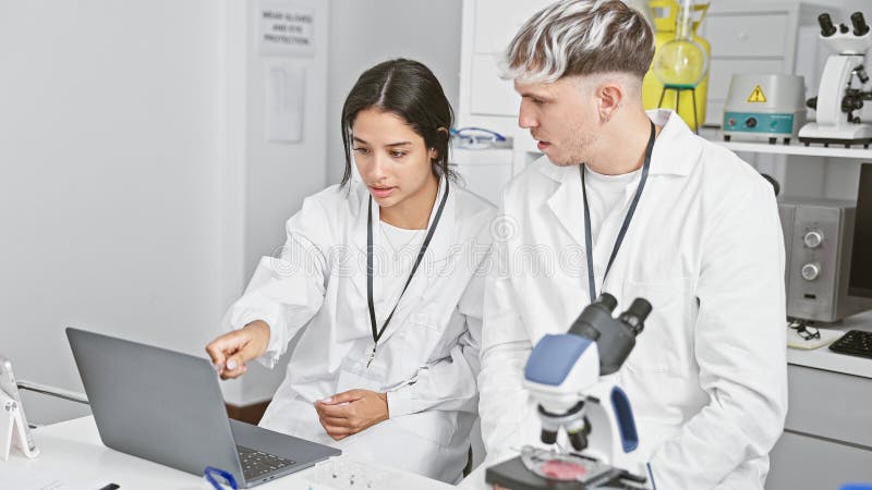 Man and Woman in Lab Coats Working As a Team Use a Laptop and Analyze Samples in the High-tech ...