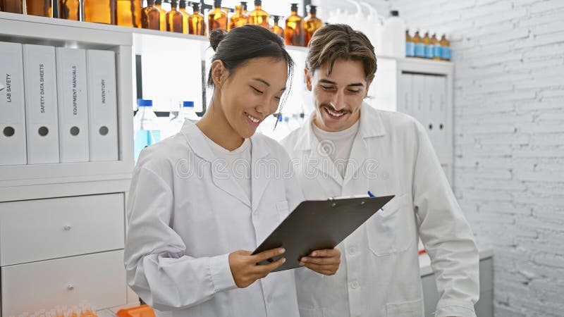 Man and Woman in White Lab Coats Smiling while Reviewing Notes in a ...