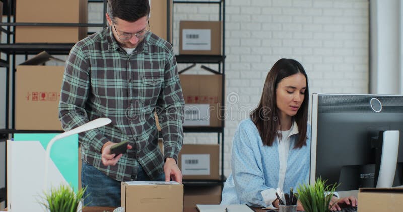 A Man and a Woman Work in a Warehouse. Young Woman Using Computer, Man ...