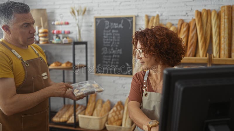 Man and Woman Working Together in a Bakery Interior, Discussing Pastries in Front of a Bread ...