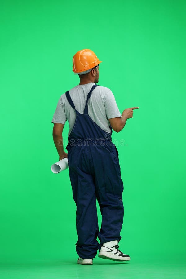 A Man in a Work Uniform on a Green Background Points To the Side, Back ...